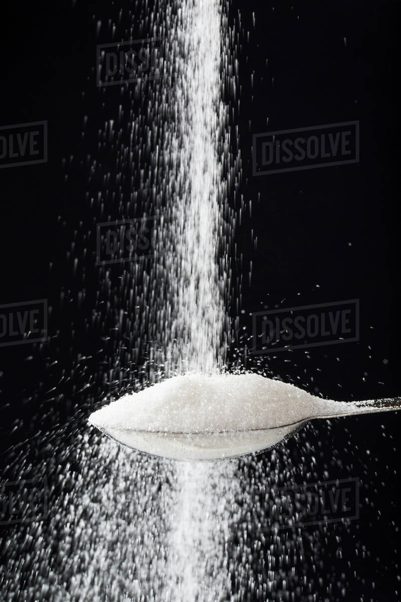 Close up of sugar falling filling a teaspoon against a black background ...