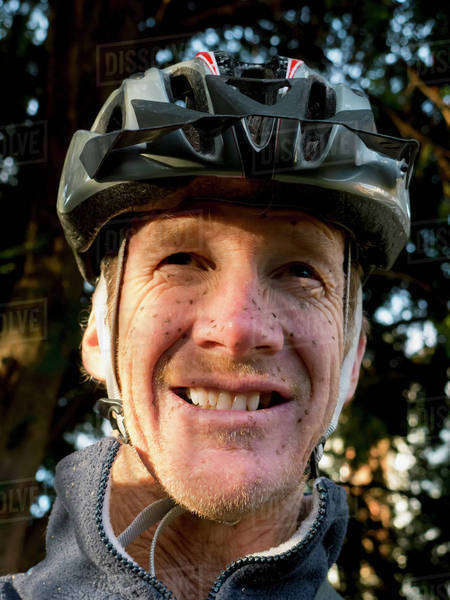 Cyclist wearing helmet with splashes of mud on his face; England ...