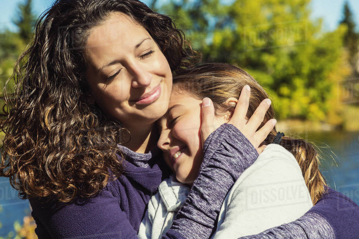 A mom hugging her daughter tightly during a family outing in a city park on a warm fall day ...