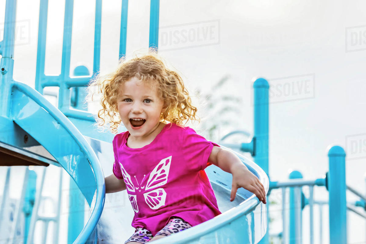 Young girl sliding down on a slide in a playground; St. Albert, Alberta ...
