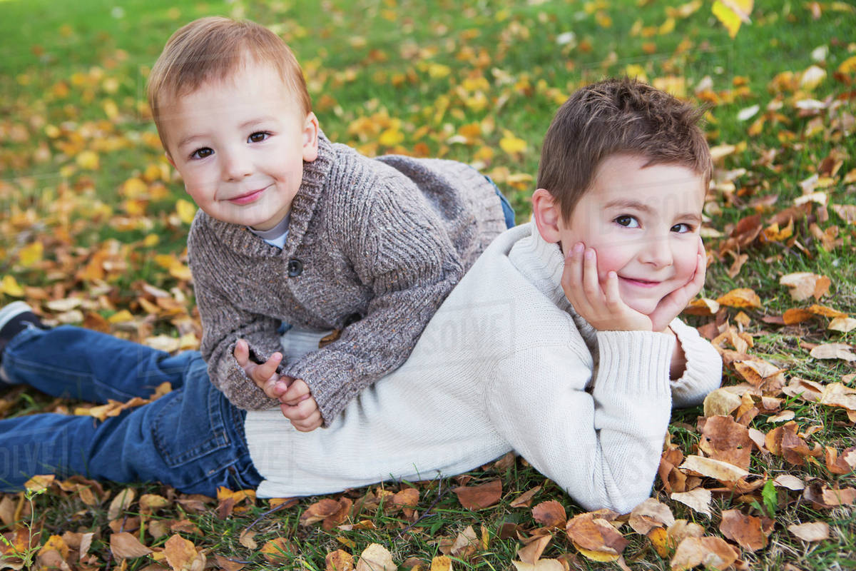 Portrait of two young boys laying on the ground in fallen autumn leaves ...