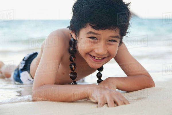 Portrait of a boy laying at the water's edge on the beach;Honolulu ...