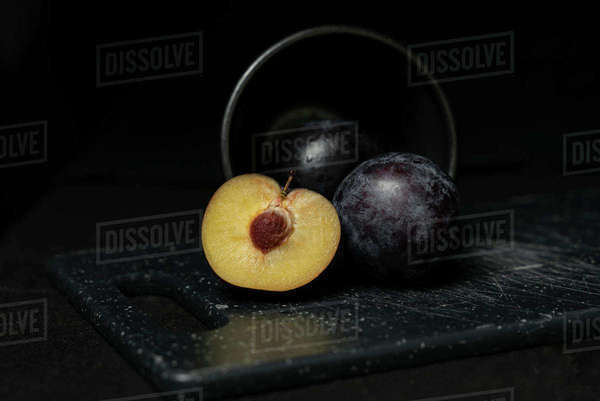 Cut plum showing an open half with a fruitstone on a black countertop ...