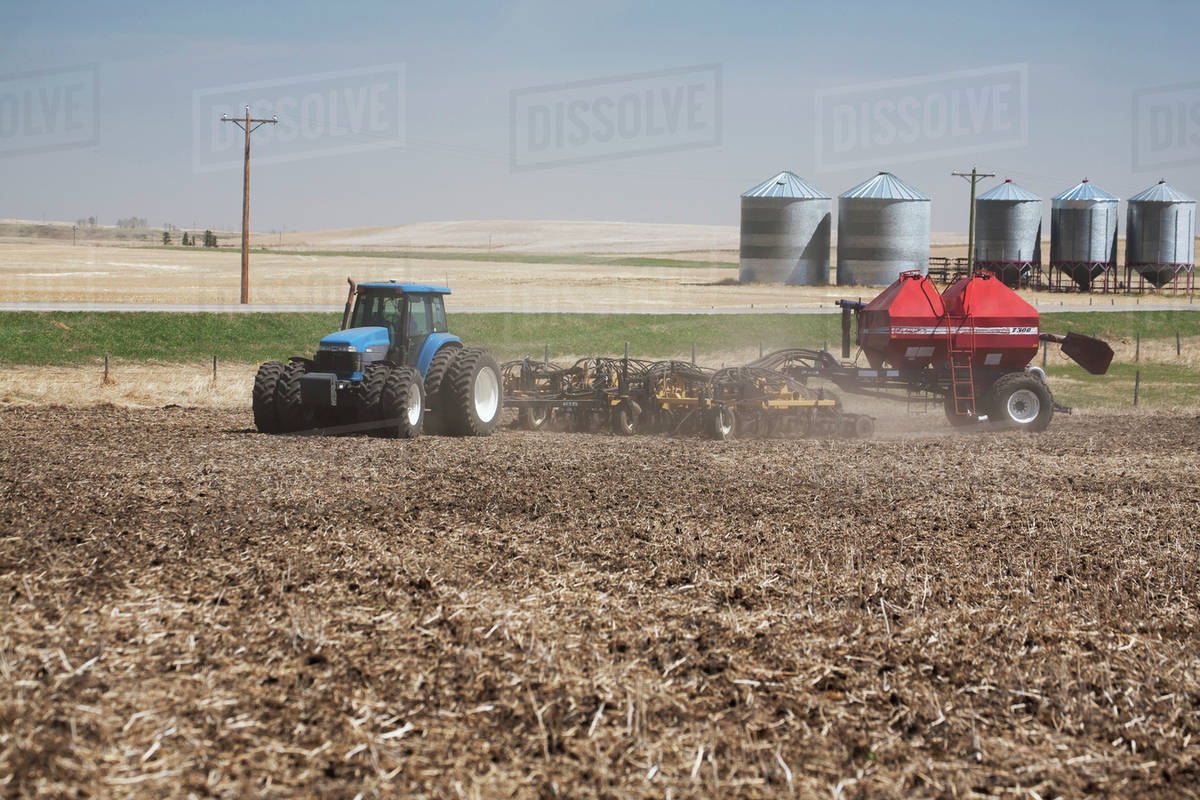 Tractor with air seeder planting crop in field with blue sky;Alberta ...