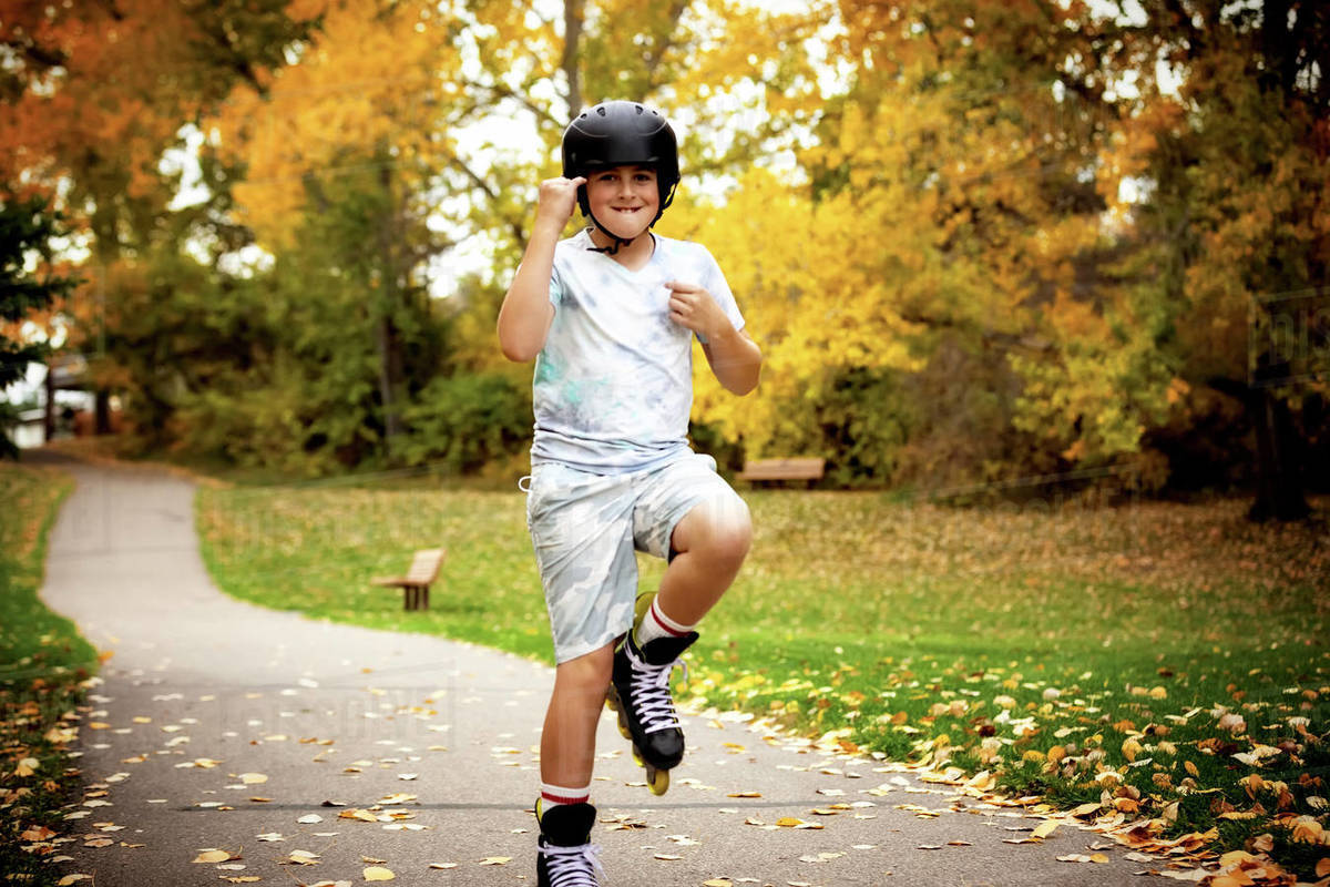 Teenage boy inline skating in a city park during a warm fall day; St ...