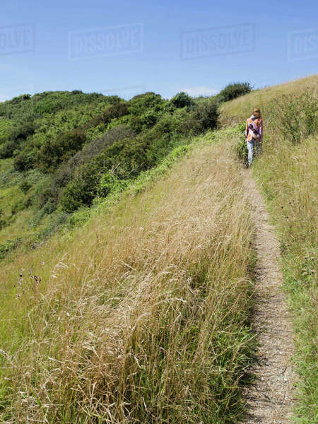 View taken from behind of a woman walking along grassy pathway on a ...