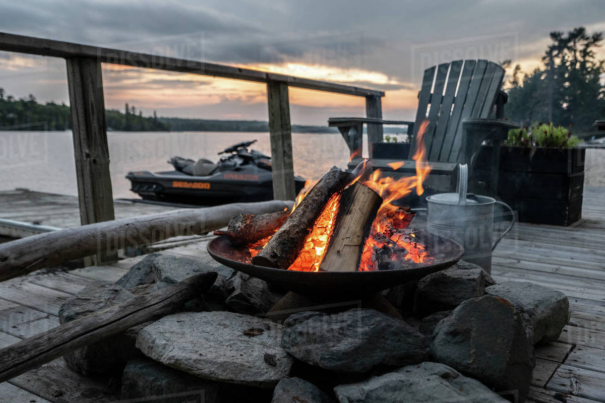 Fire burning in a fire pit on a dock at twilight; Lake of the Woods ...