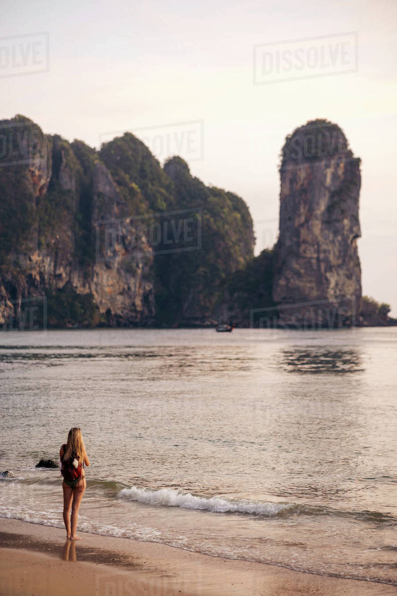 Female tourist in a swimsuit enjoys the rugged beauty of the rocky ...