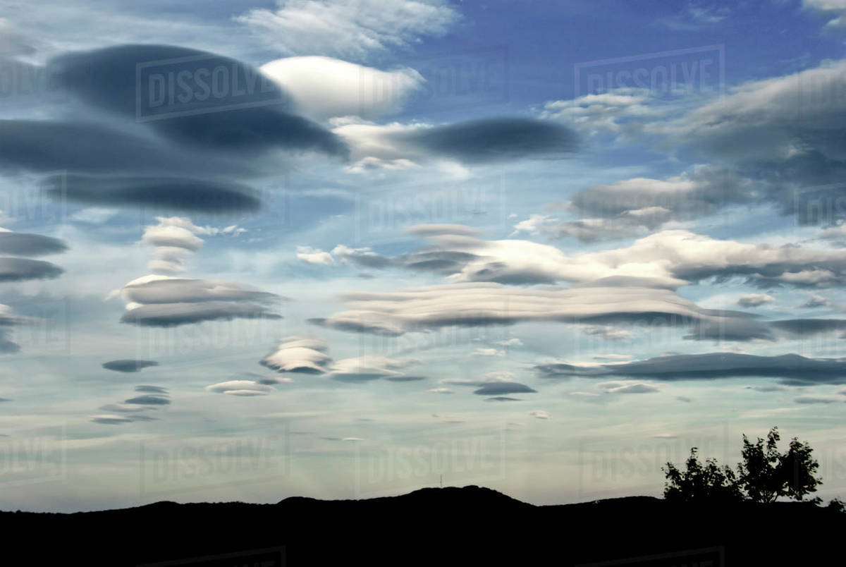 Lenticular clouds form over mountains. Anticrepuscular rays rise up to ...