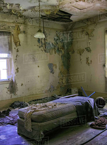 Abandoned bed in a decrepit room with damaged ceiling and walls and ...