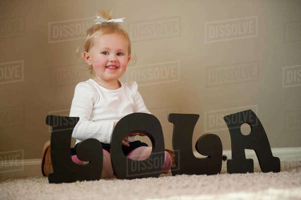 Smiling toddler girl sits behind letters spelling her name, Lola ...