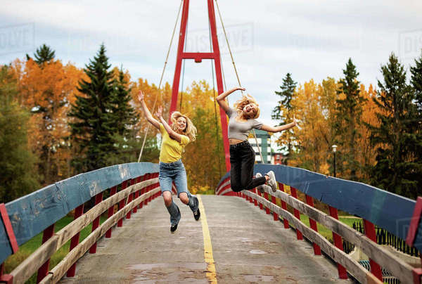 Two teenage girls running across a bridge and jumping in the air in a ...