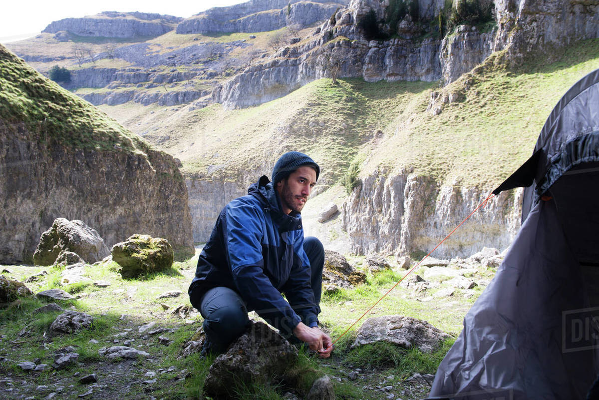 A mountaineer pitching his tent in rugged terrain. - Stock Photo - Dissolve