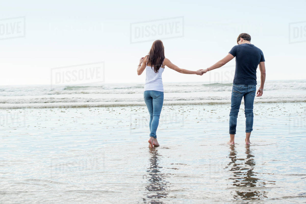 A young couple walk holding hands across the beach at Porthmadog ...