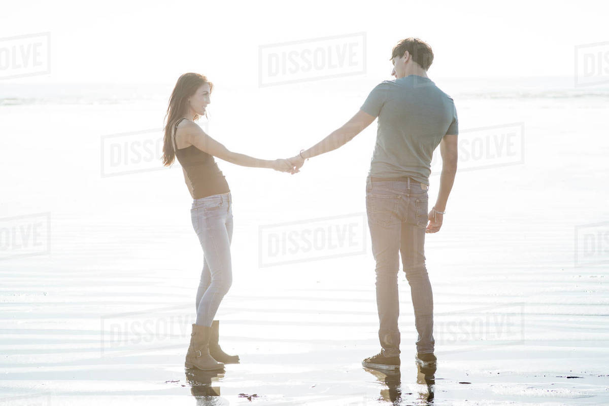 A young couple walk holding hands across the beach at Porthmadog ...