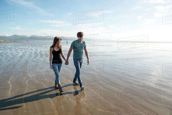 A young couple walk holding hands across the beach at Porthmadog ...