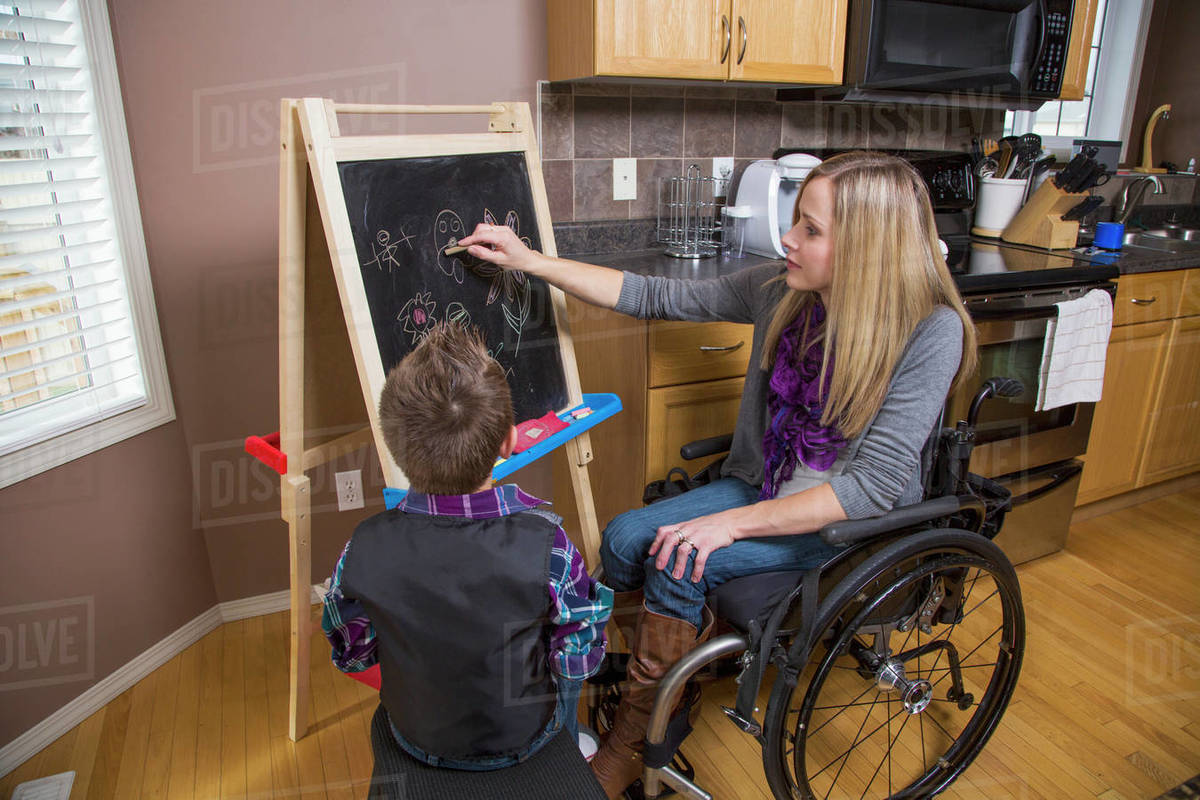 Young paraplegic mother teaching her son and drawing on a chalkboard ...