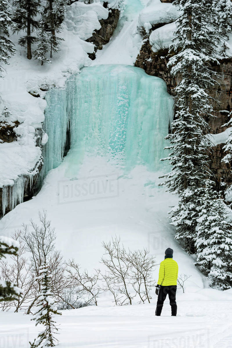 Female snowshoeing along a snow-covered trail with an ice falls on a ...