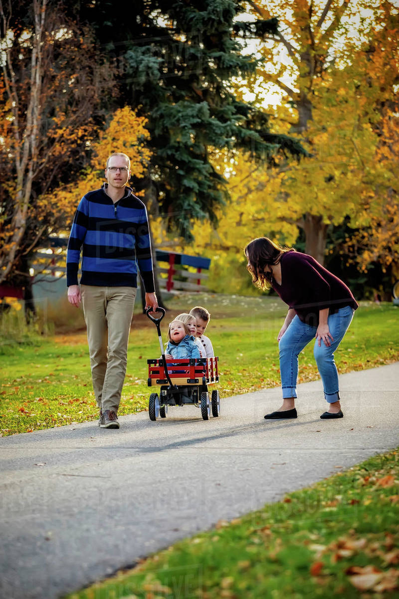 A father and mother pulling their young children in a wagon in a city ...