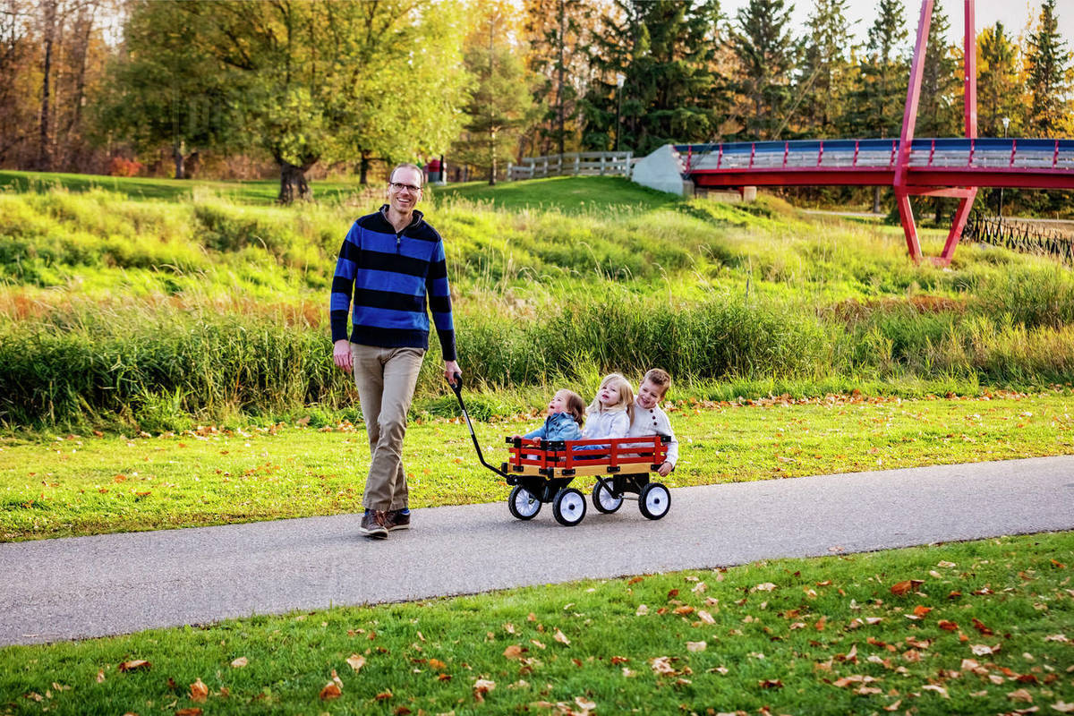 A father pulling his young children in a wagon along a river in a city ...