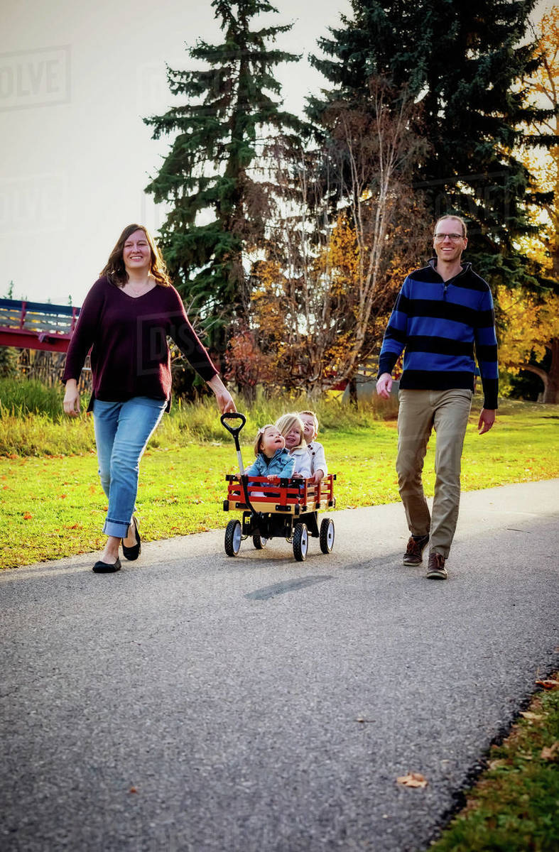 A father and mother pulling their young children in a wagon in a city ...
