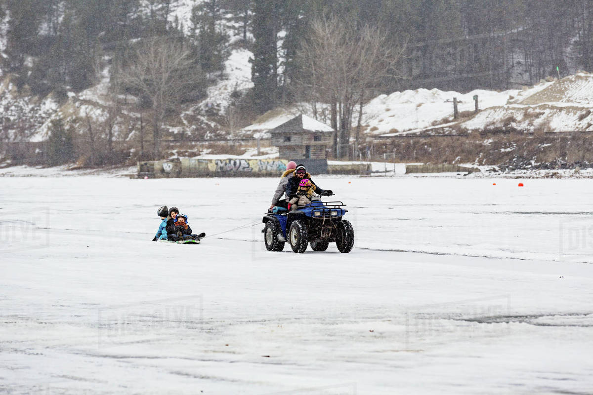 A Woman And Man Riding An ATV And Pulling A Sled On A Frozen Lake With ...