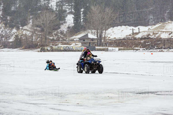 A Woman And Man Riding An ATV And Pulling A Sled On A Frozen Lake With ...