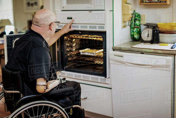 Man with double limb amputations using the oven in the kitchen at home ...