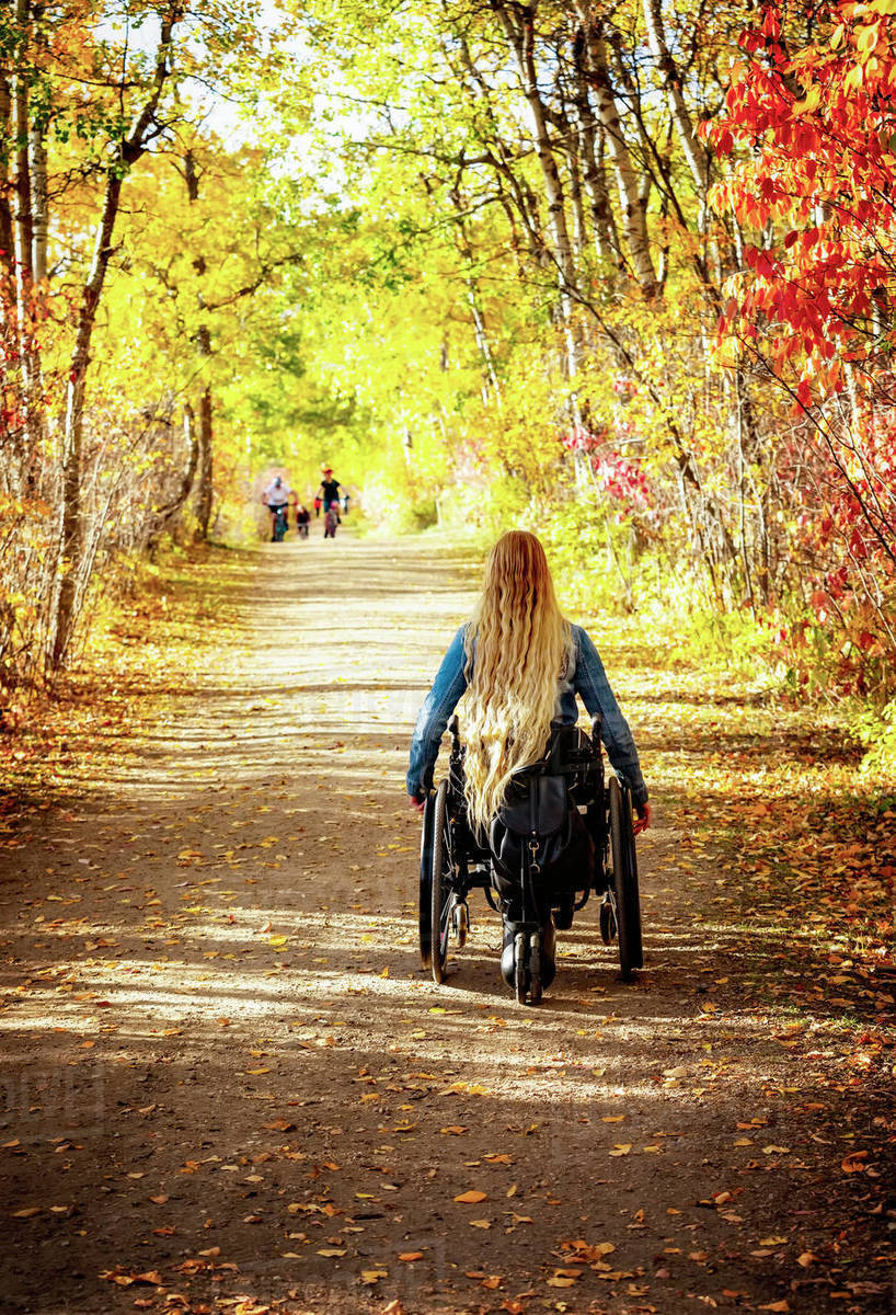 Young paraplegic woman in her wheelchair going down a trail in a park ...