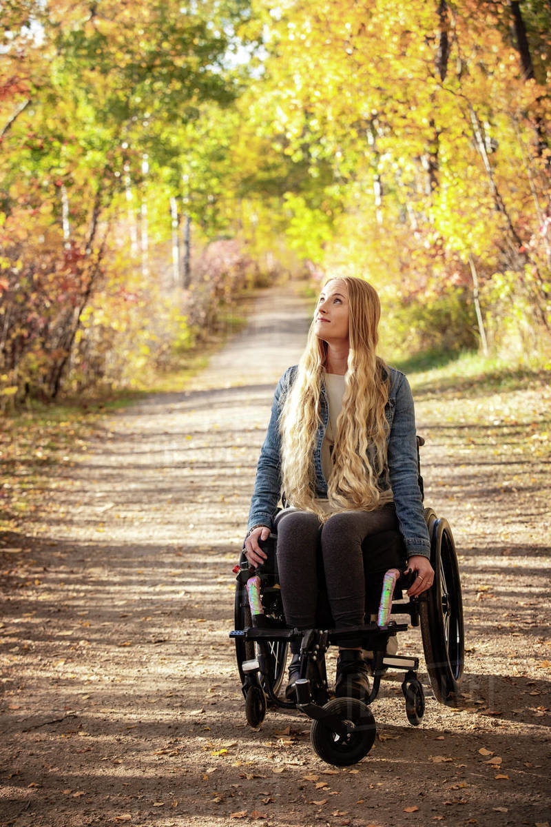 Young paraplegic woman in her wheelchair going down a trail in a park ...