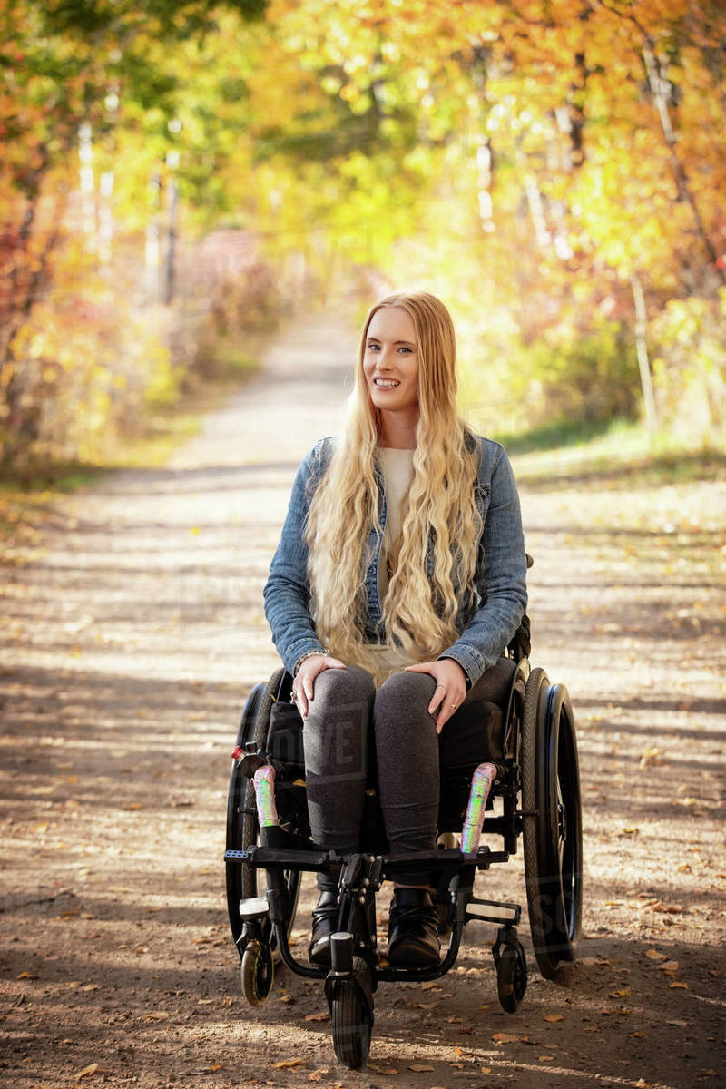 Young paraplegic woman in her wheelchair going down a trail in a park ...
