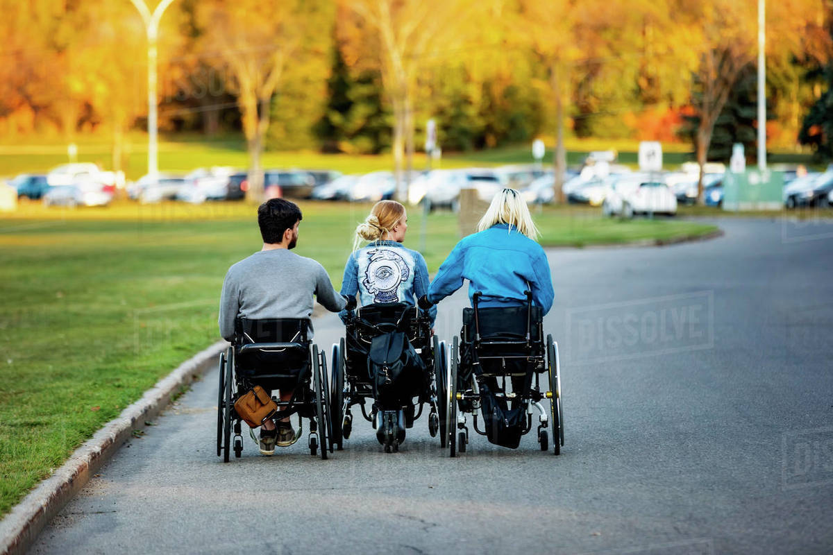 Three young paraplegics in their wheelchairs going through a parking ...