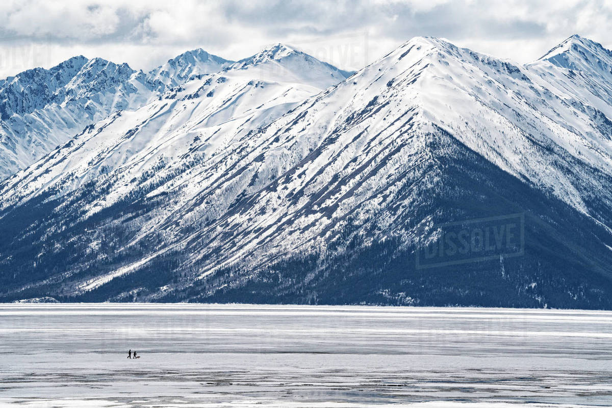 Two people walking with their dog on the frozen Bennett Lake during ...
