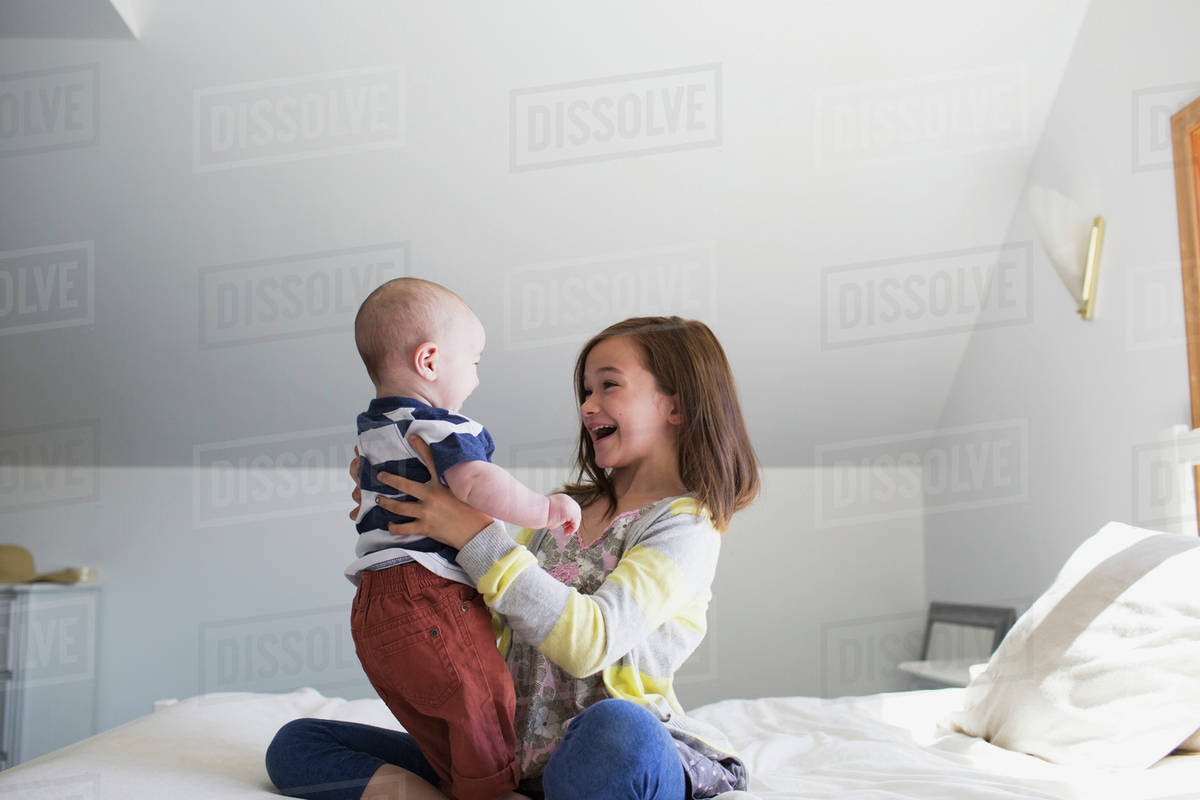 A sister playing with her baby brother on a bed at home; Victoria ...