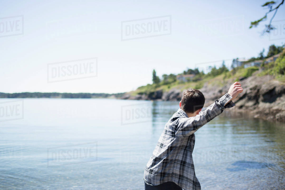 A boy throws rocks into the water; Victoria, British Columbia, Canada ...