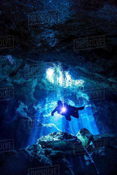A cave diver descends into a cave system with light rays penetrating ...