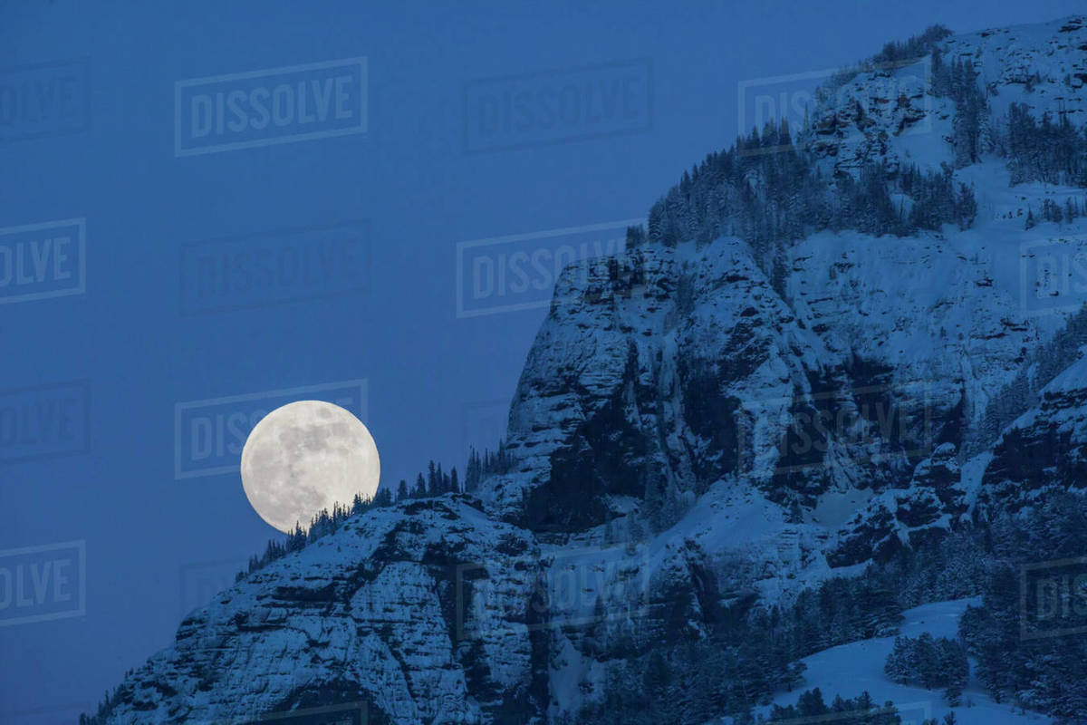 Full Moon rising in a blue, night sky behind a mountain cliff in Lamar ...