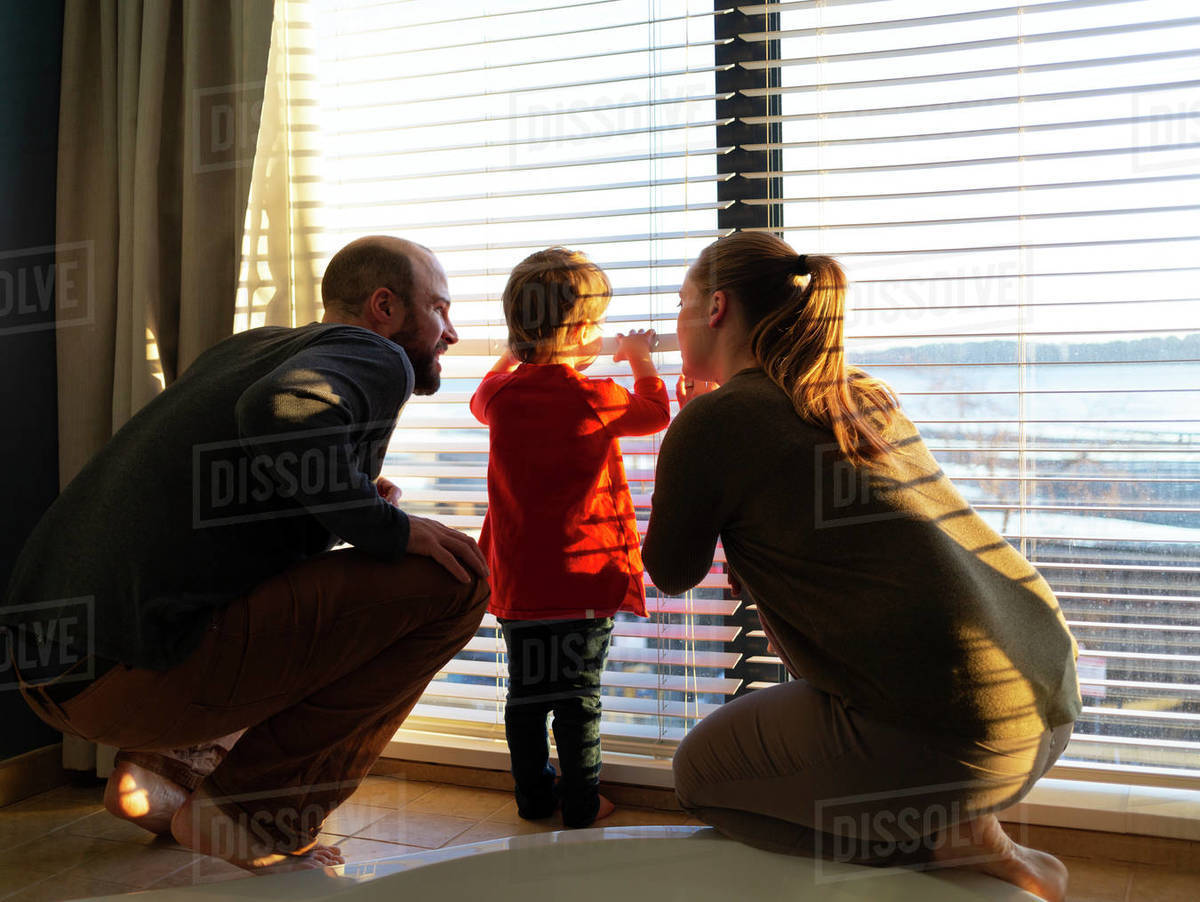 A young mother and father crouch by their toddler daughter to look out ...