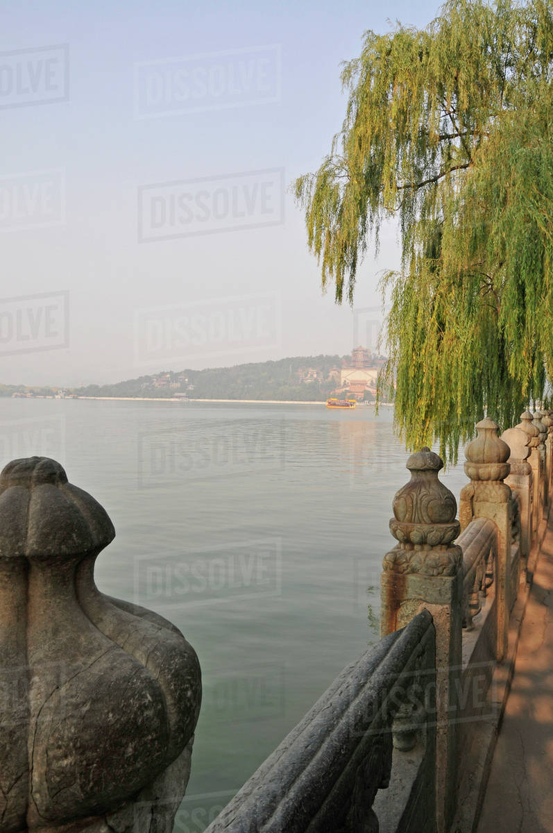 A tree and ornate balusters on a railing on the water's edge;Beijing ...