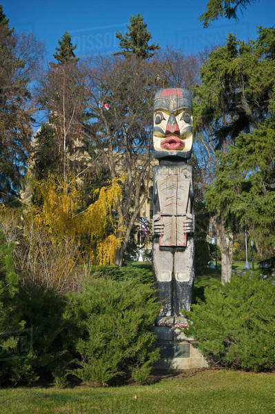 Totem pole amongst trees with legislative building in the background ...