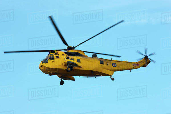 A Yellow Helicopter Flying In A Blue Sky; Northumberland, England ...