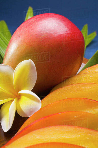 Studio Shot Of Mango, Whole And Cut Into Slices, With Flowers ...