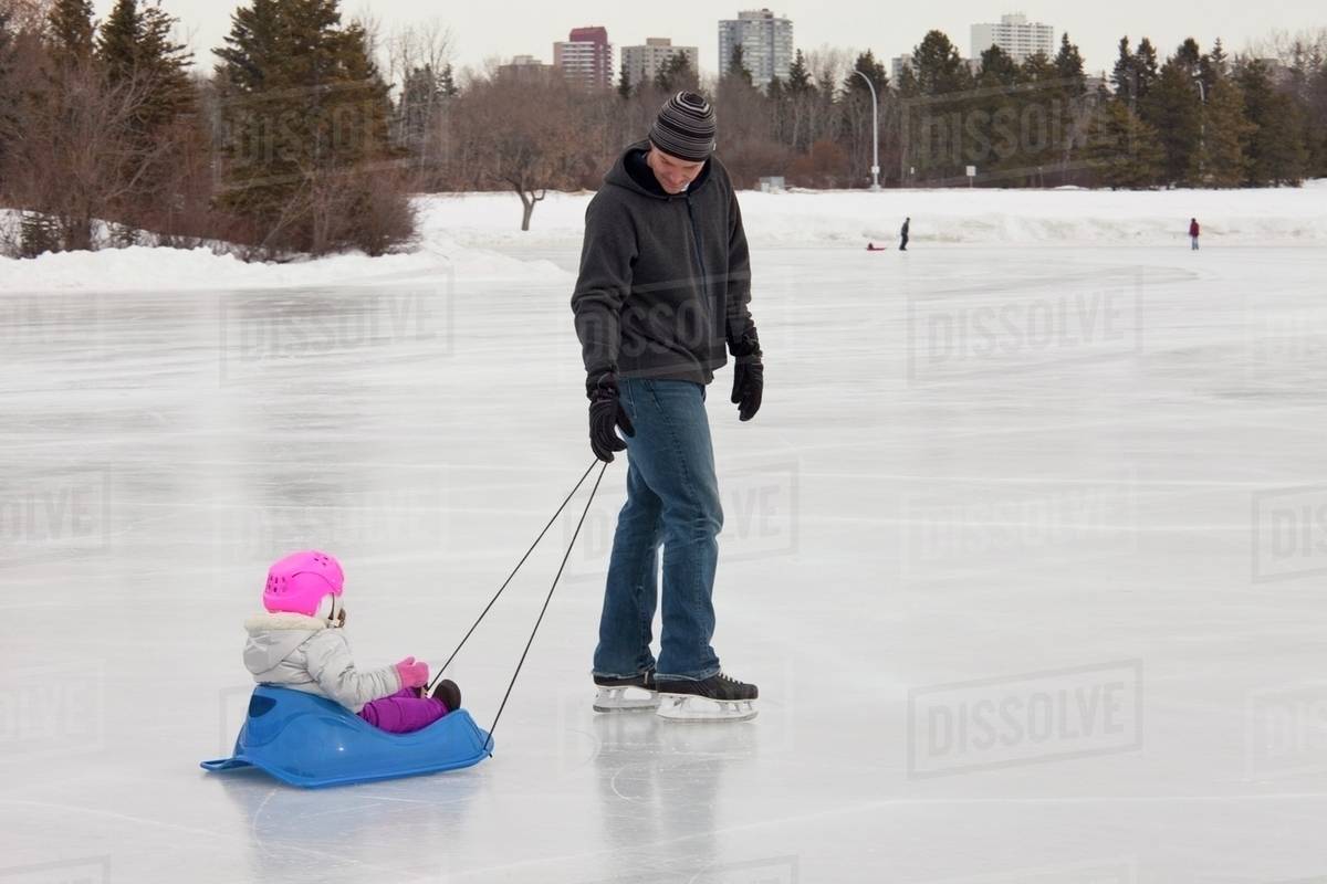 A Father Pulls His Young Daughter In A Sled Over An Outdoor Ice Rink ...