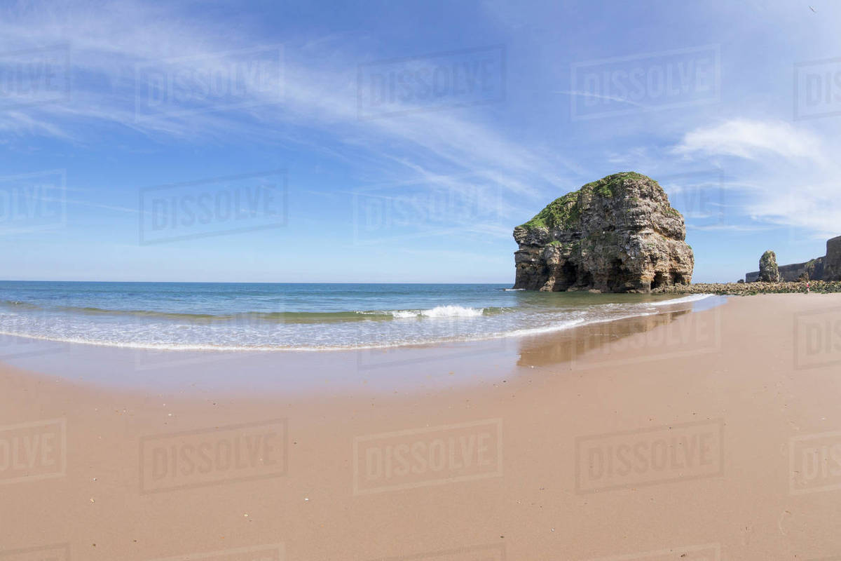 Large rock formation on a beach with water washing up on the sand ...