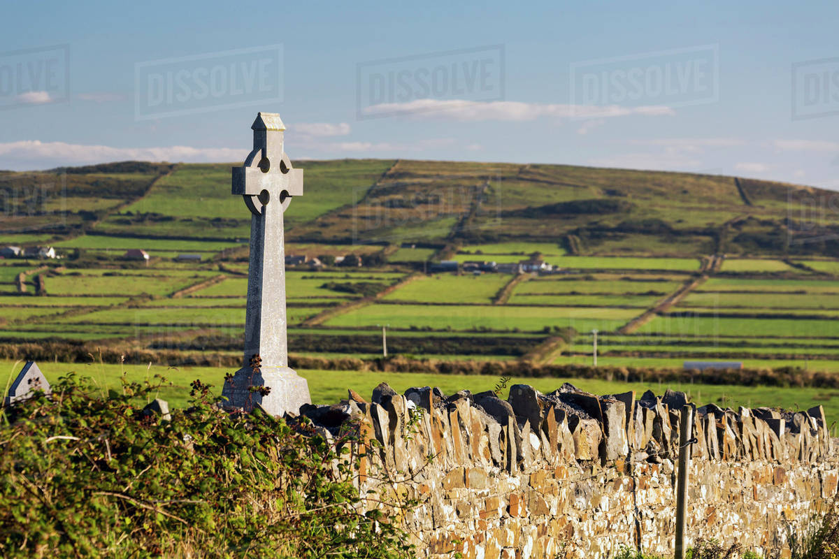 Celtic cross with stone fence and hilly grass fields in the distance ...