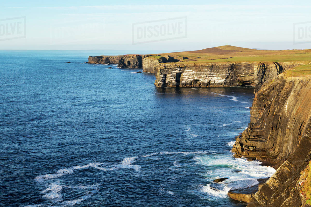 Dramatic rock cliffs along the shoreline at sunset with blue sky ...