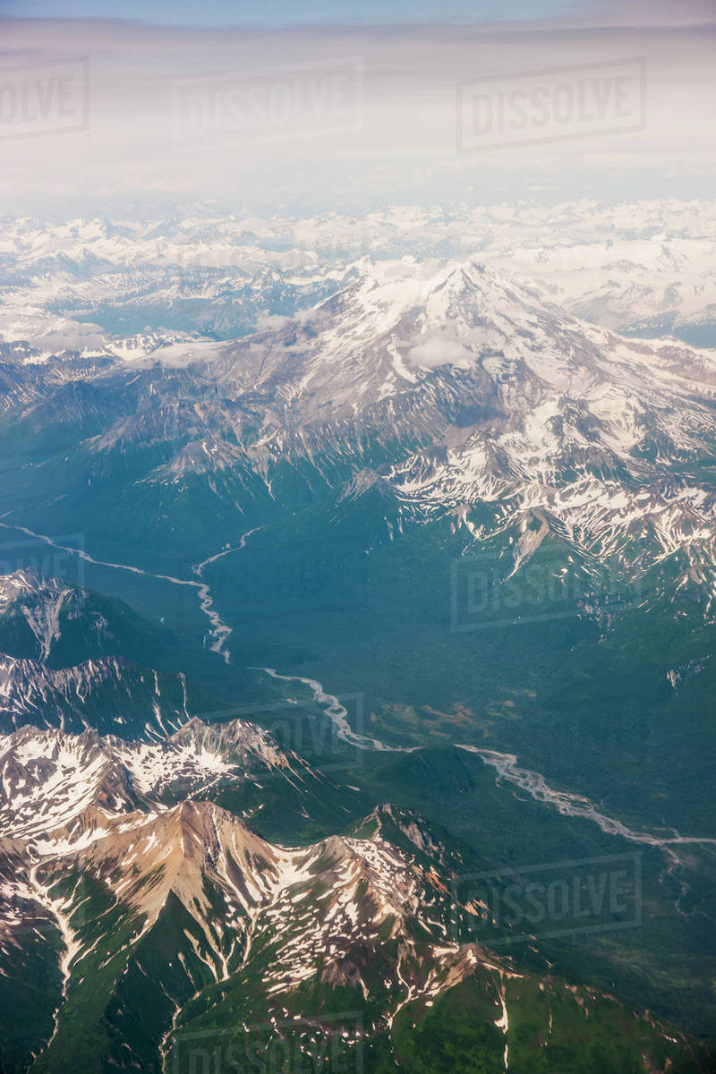Aerial view of snow-capped peaks surrounding a green river valley ...