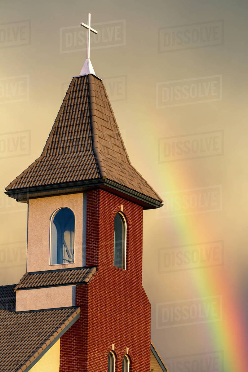 Church steeple with orange glow from the sunset and rainbow in the sky ...