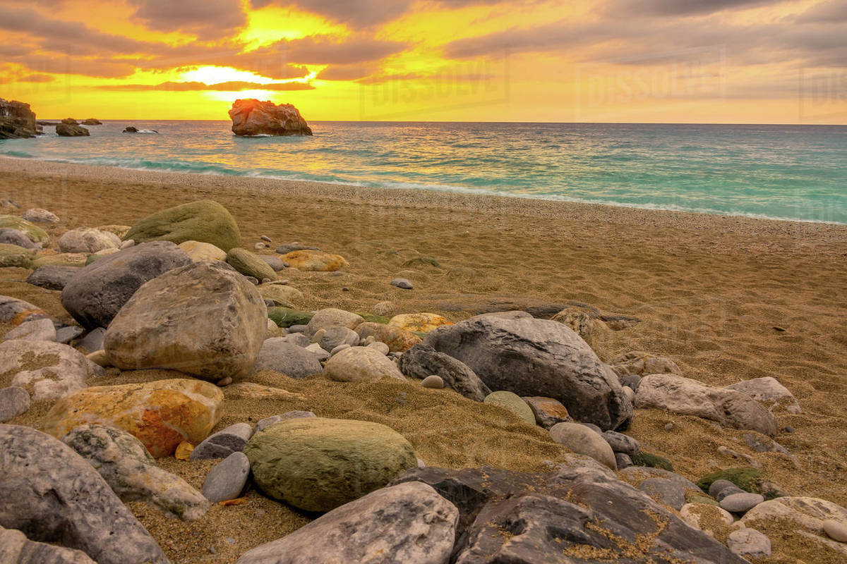 Coarse sand beach with colorful stones. Golden sunset over the calm sea ...