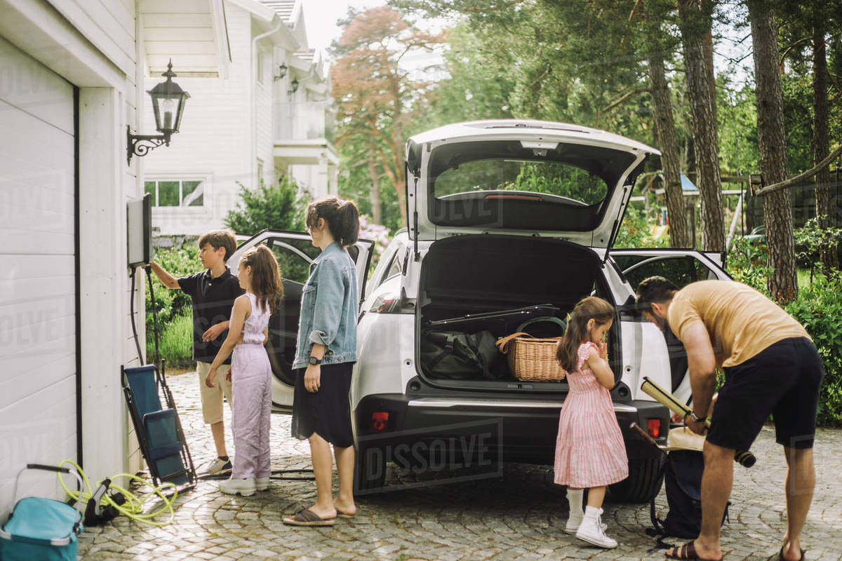 Family charging and loading luggage in trunk of electric car outside ...